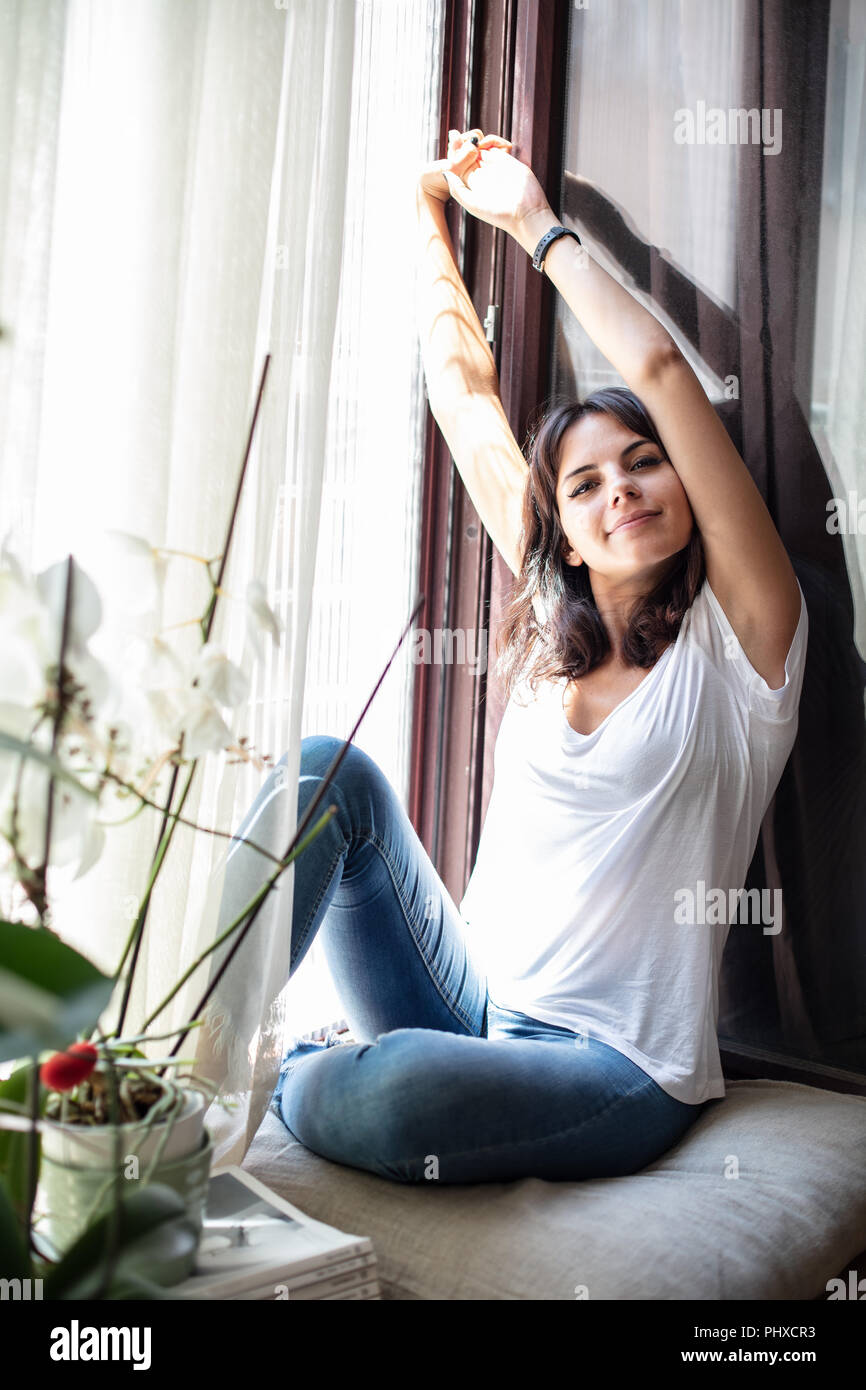 Relaxed young woman stretching her arms above her head as she relaxes ...