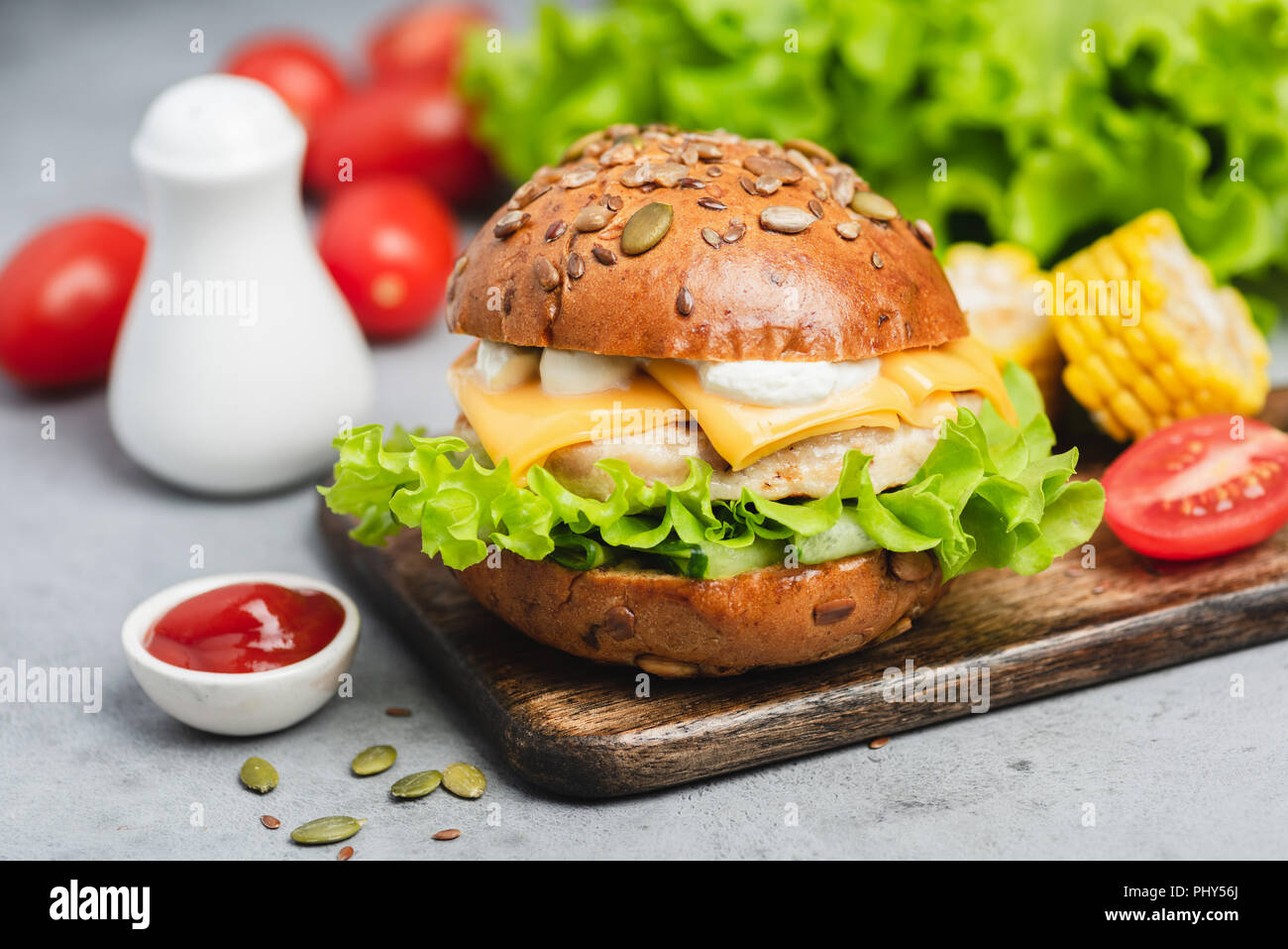 Chicken cheeseburger on wooden serving board on concrete background ...