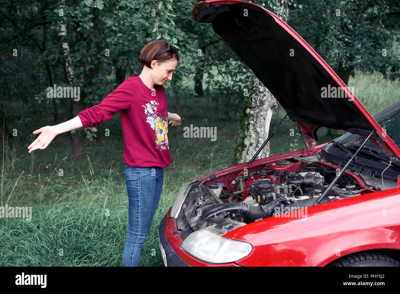 a young girl stands at a broken car and looks at the engine, does not ...