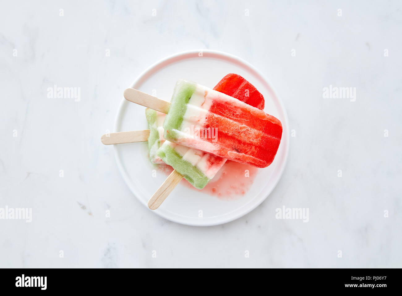 A stack of berry melting ice cream lolly in a white plate on a gray ...
