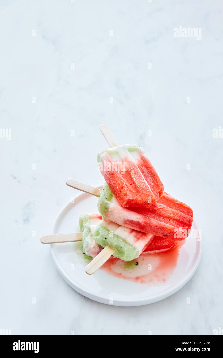 Plate with red fruity ice cream lolly with splashes on a gray marble ...