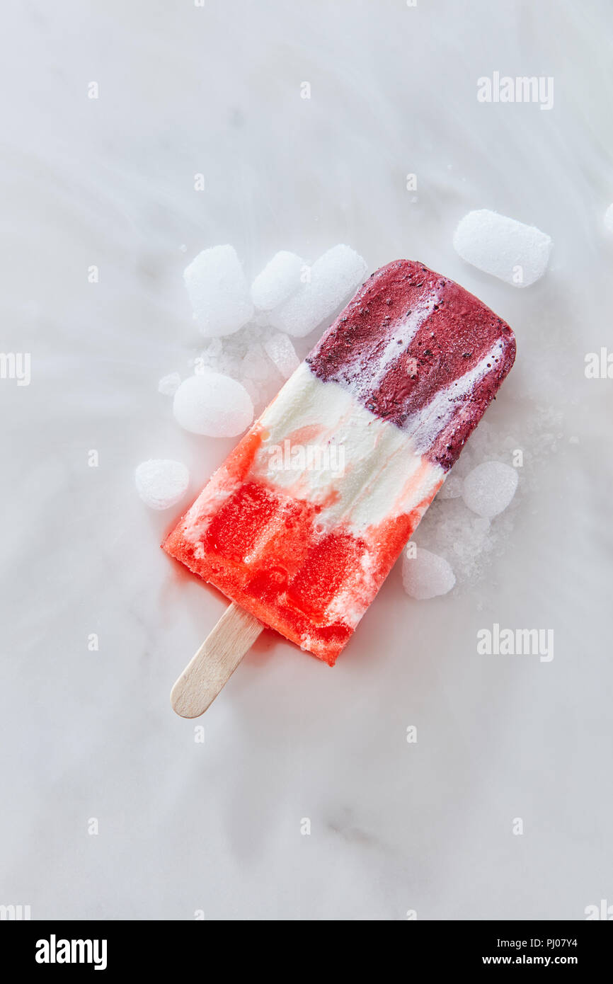 Vanilla berry sorbet on a stick with ice slices on a gray marble ...