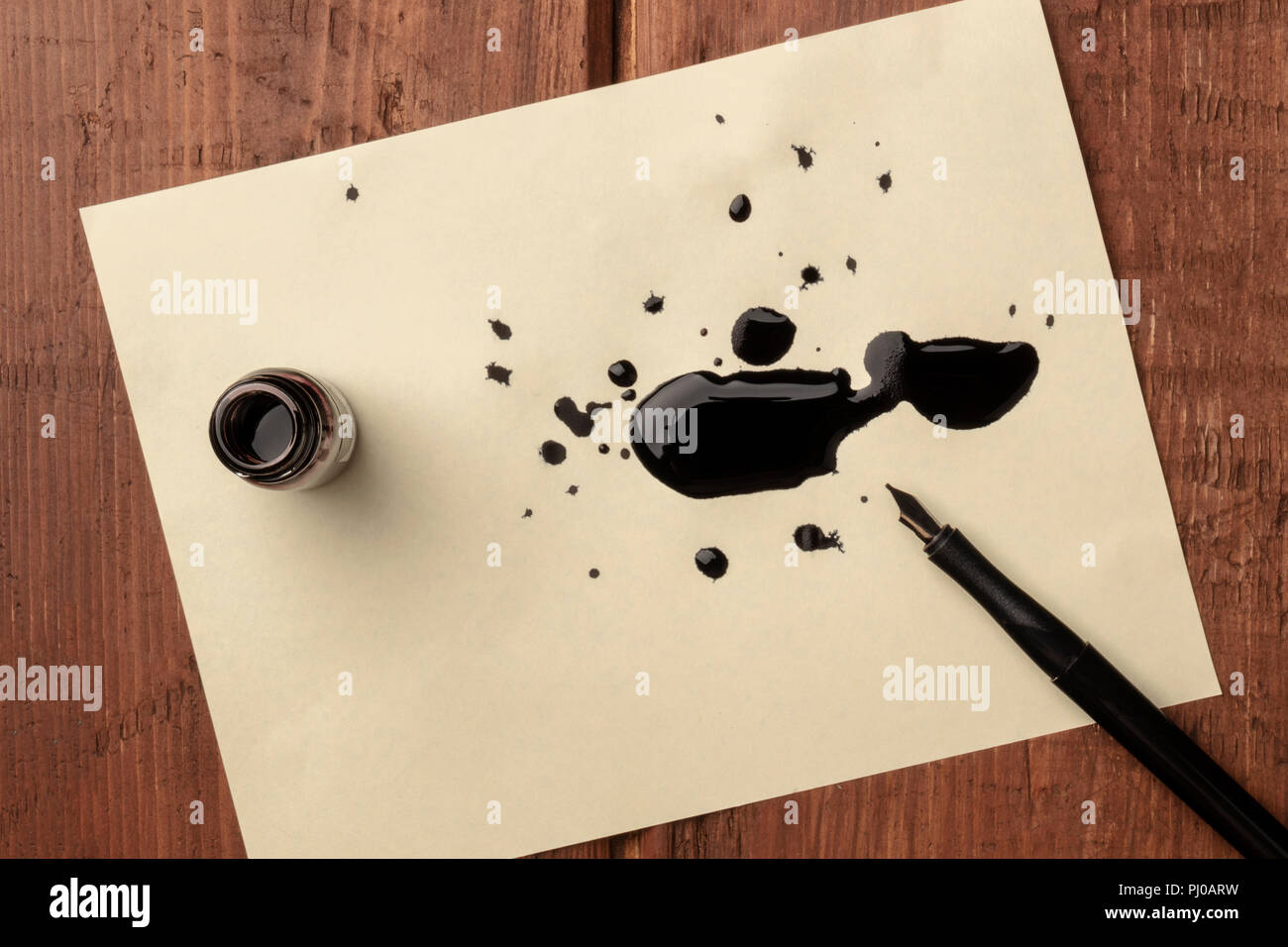 An overhead photo of an ink well with drops of ink and a nib pen, with ...
