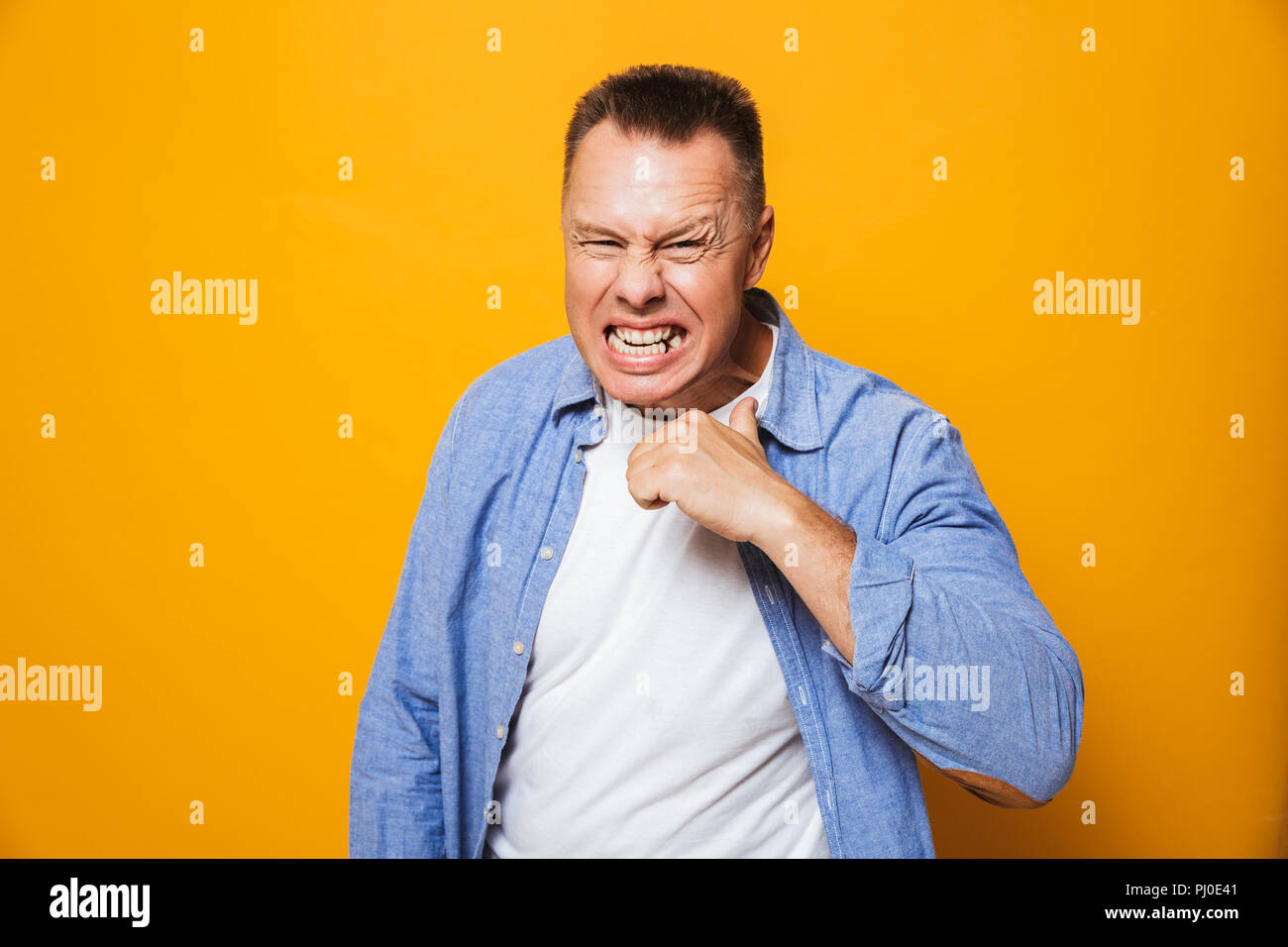 Portrait of an angry middle aged man threatens you isolated over yellow ...