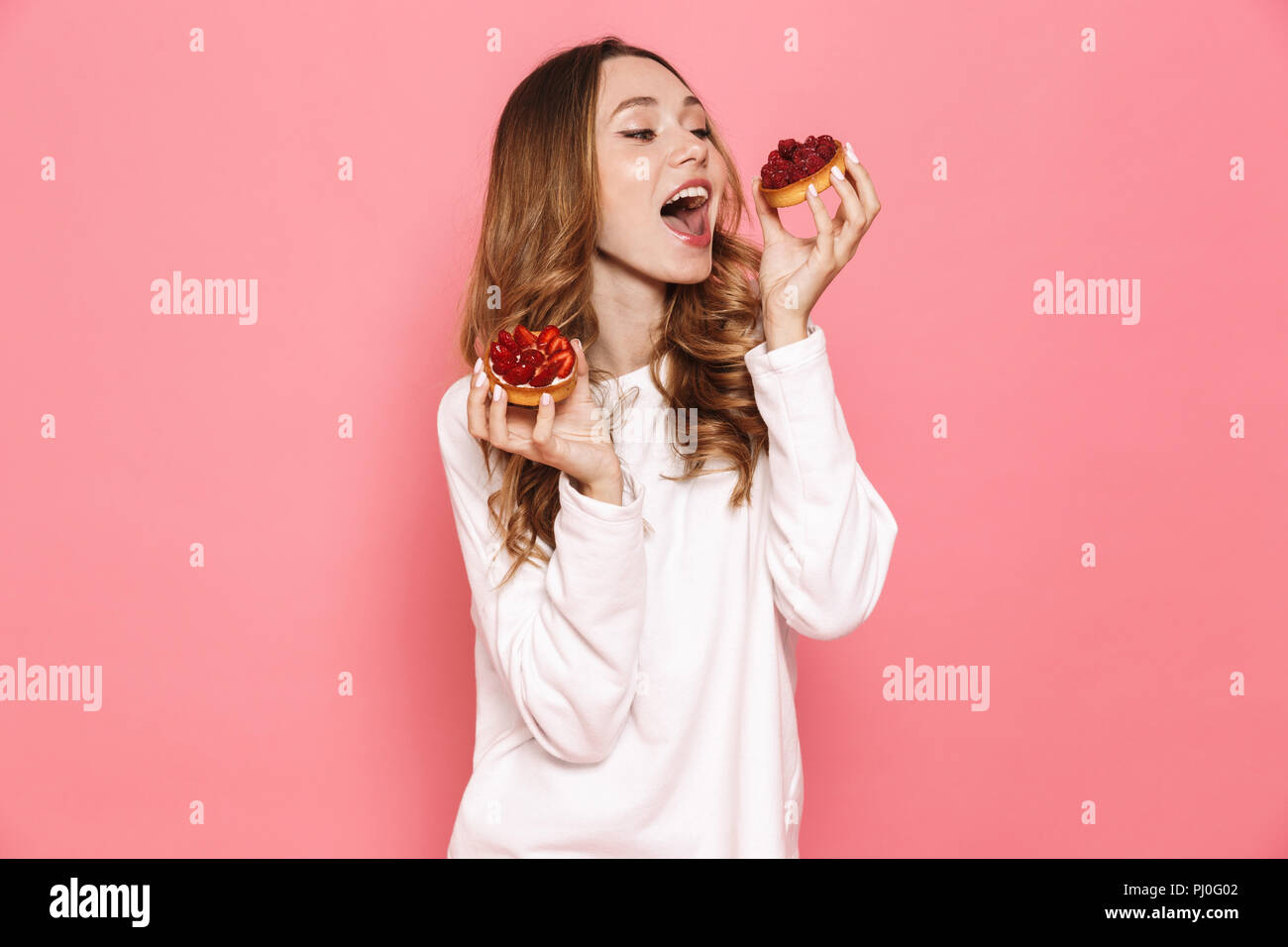 Portrait of a satisfied young woman eating pastry isolated over pink ...