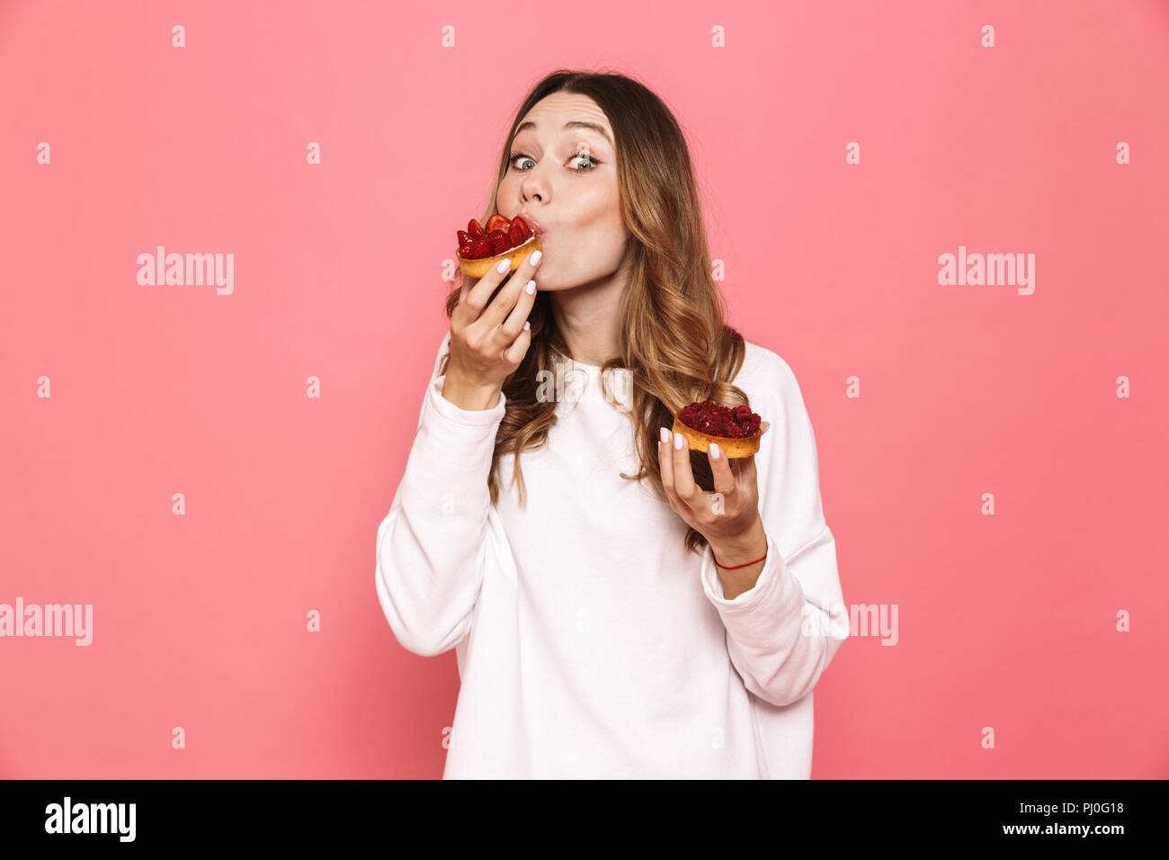 Portrait of a satisfied young woman eating pastry isolated over pink ...