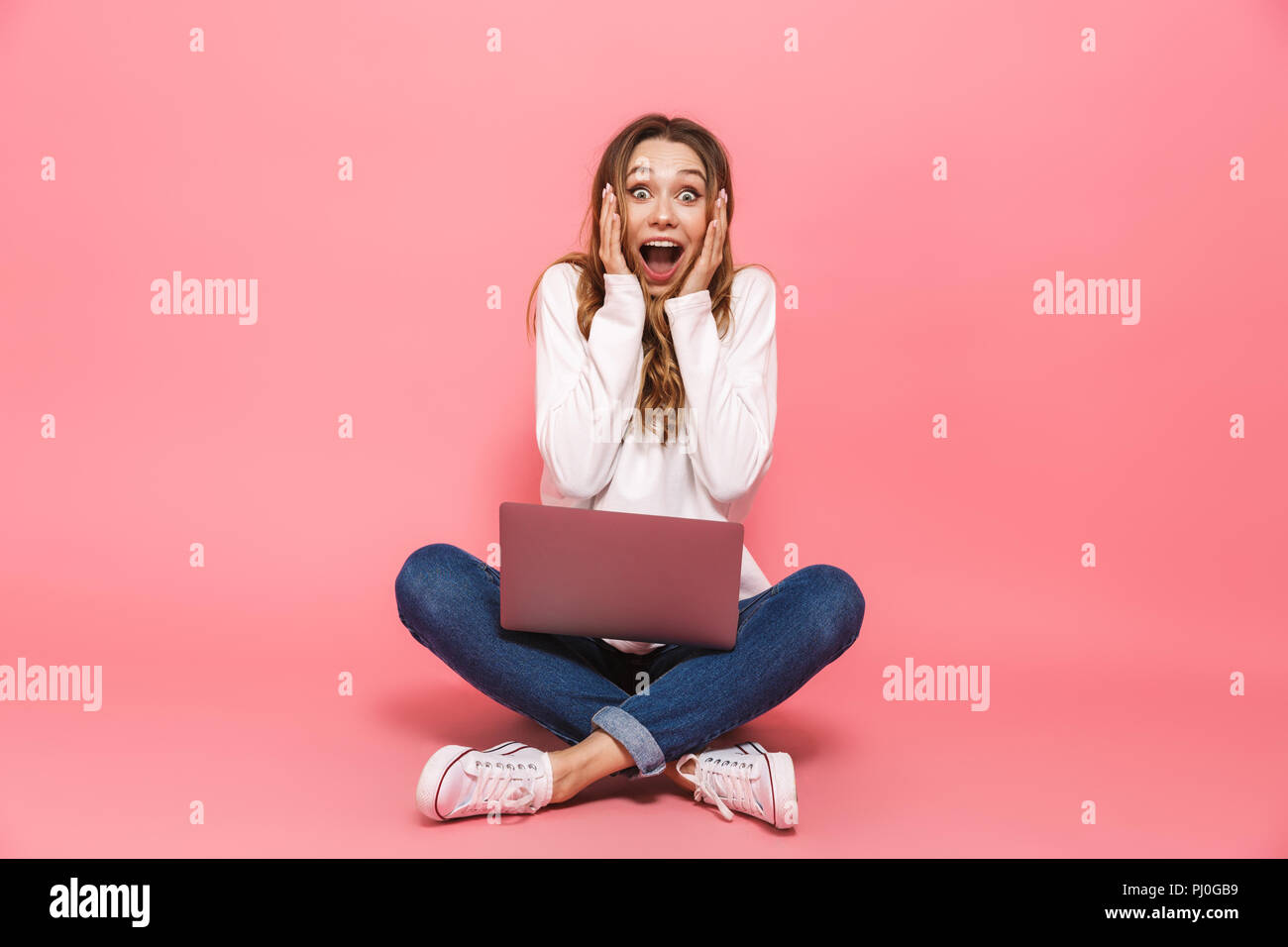 Portrait of a shocked young woman sitting with legs crossed, using ...