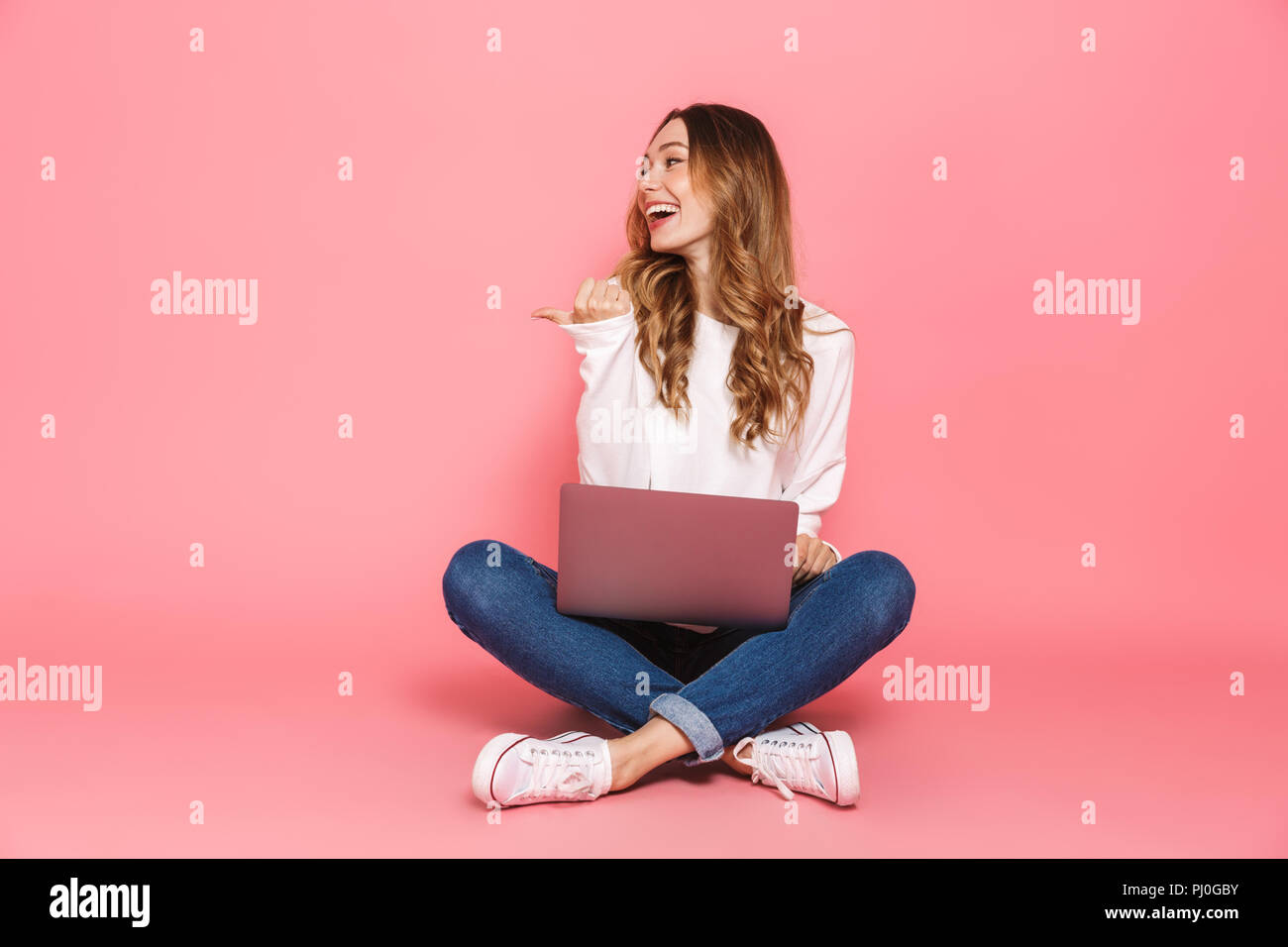 Portrait of a joyful young woman sitting with legs crossed, using ...