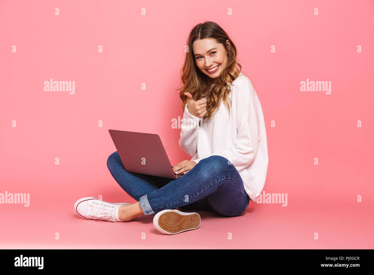 Portrait of a smiling young woman sitting with legs crossed, using ...