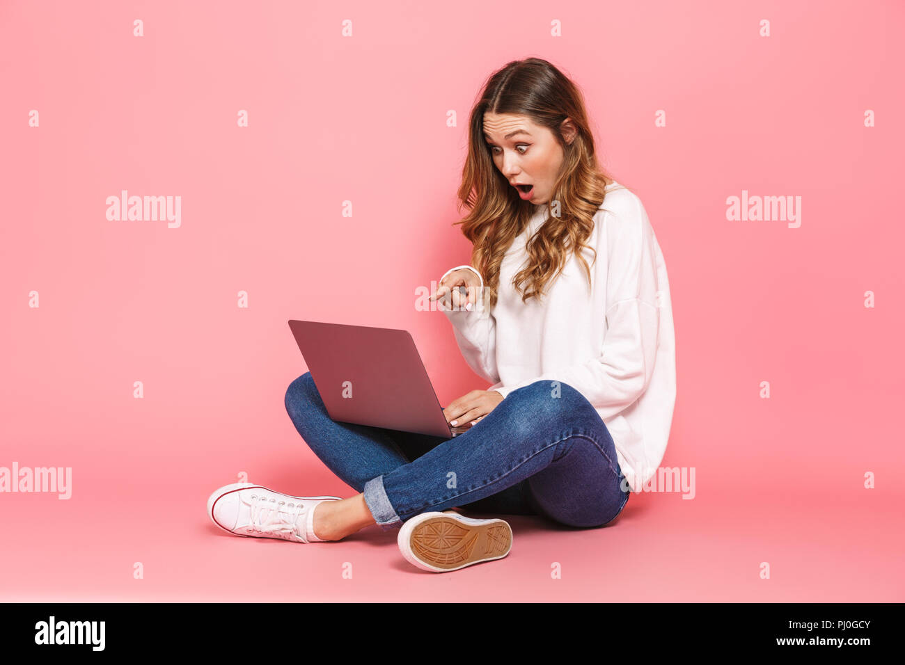 Portrait of a smiling young woman sitting with legs crossed, using ...