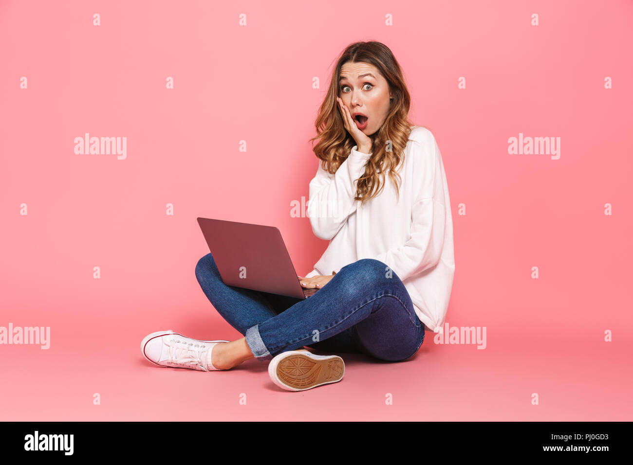 Portrait of a shocked young woman sitting with legs crossed, using ...