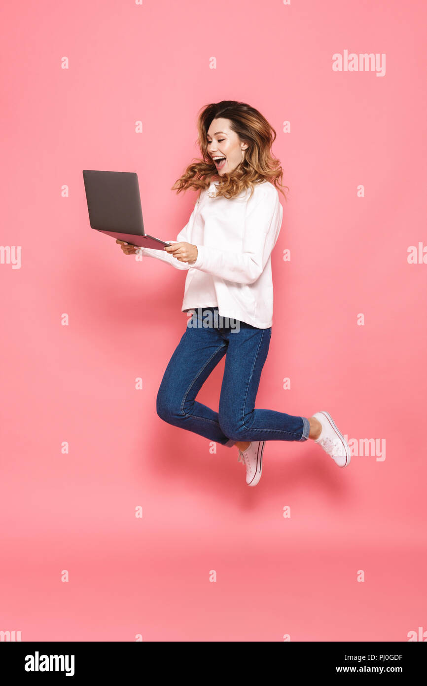 Full length portrait of a happy young woman jumping, using laptop ...