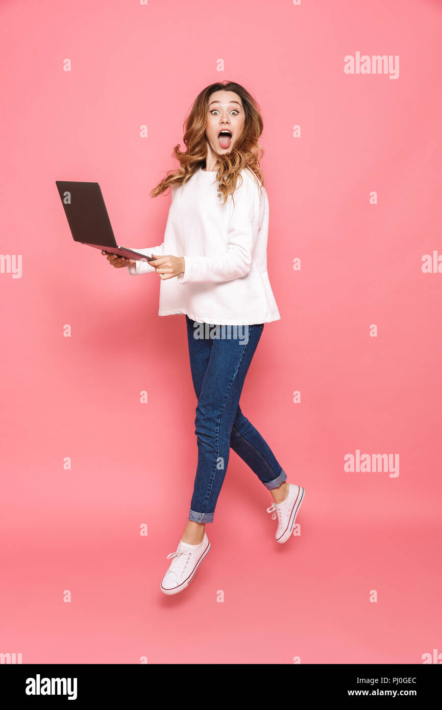 Full length portrait of a shocked young woman jumping, using laptop ...