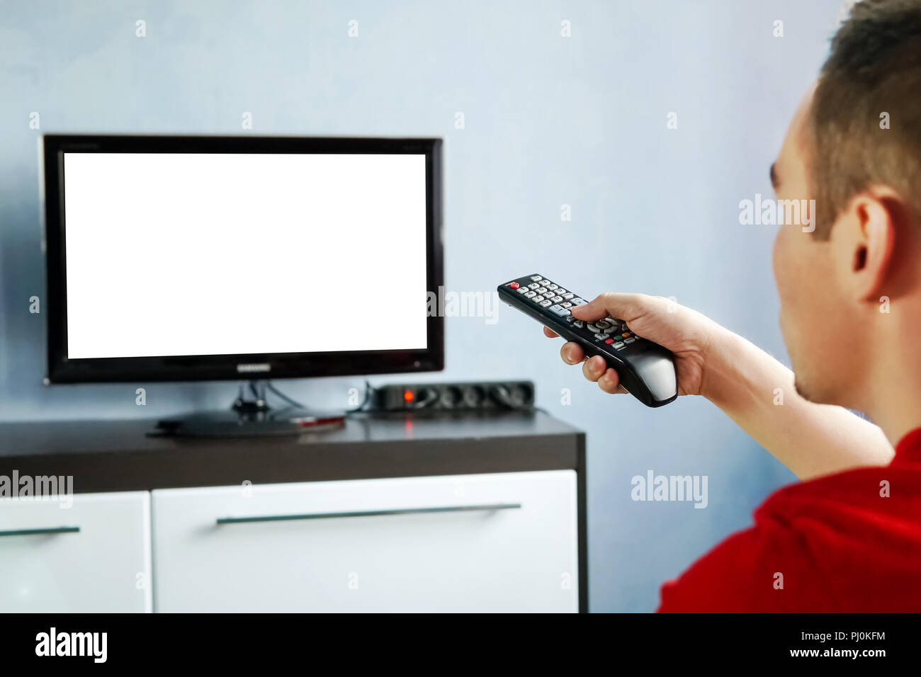 TV remote control in male hand in front of widescreen TV set with blank ...