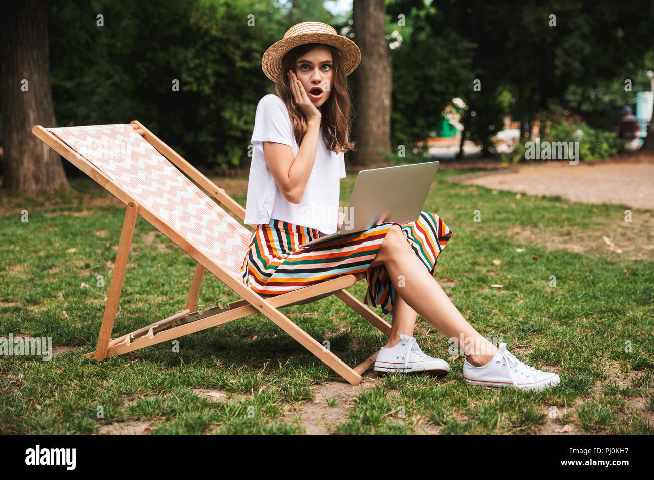 Shocked young girl sitting with laptop computer at the park outdoors ...
