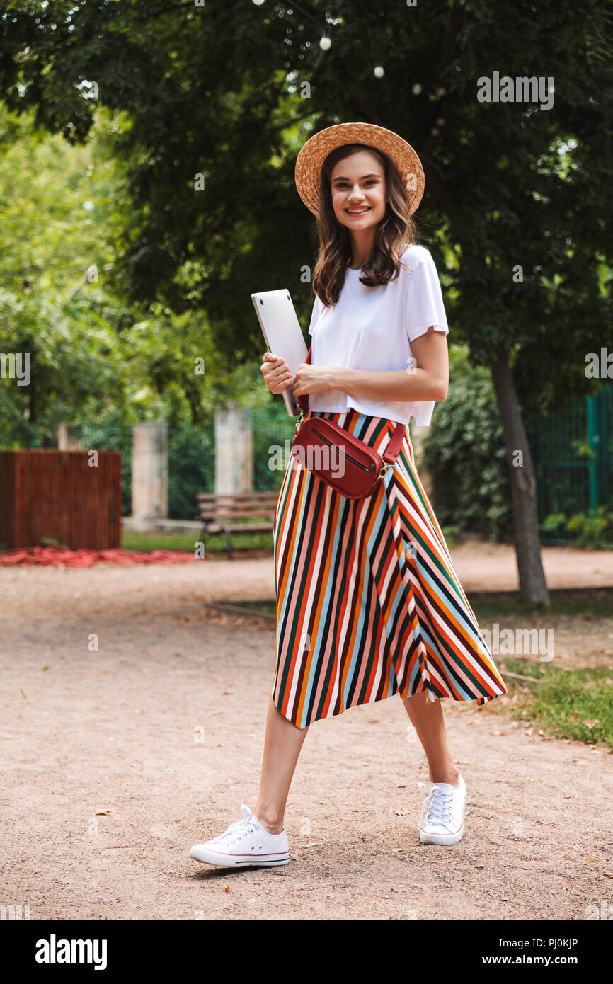 Smiling young girl walking with laptop computer at the park outdoors ...