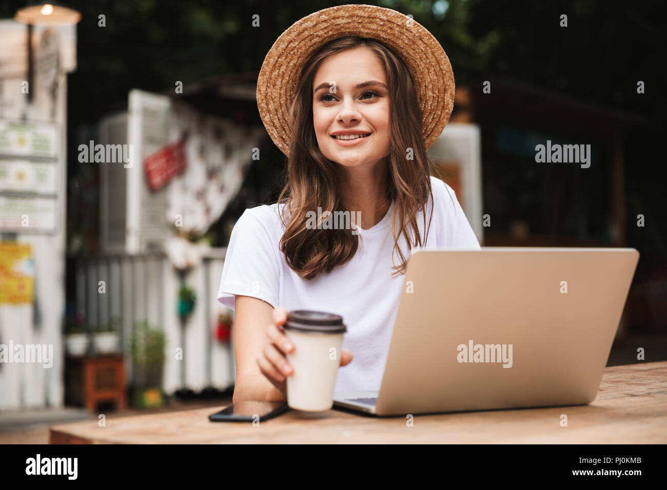 Happy young girl drinking coffee while sitting with laptop computer at ...