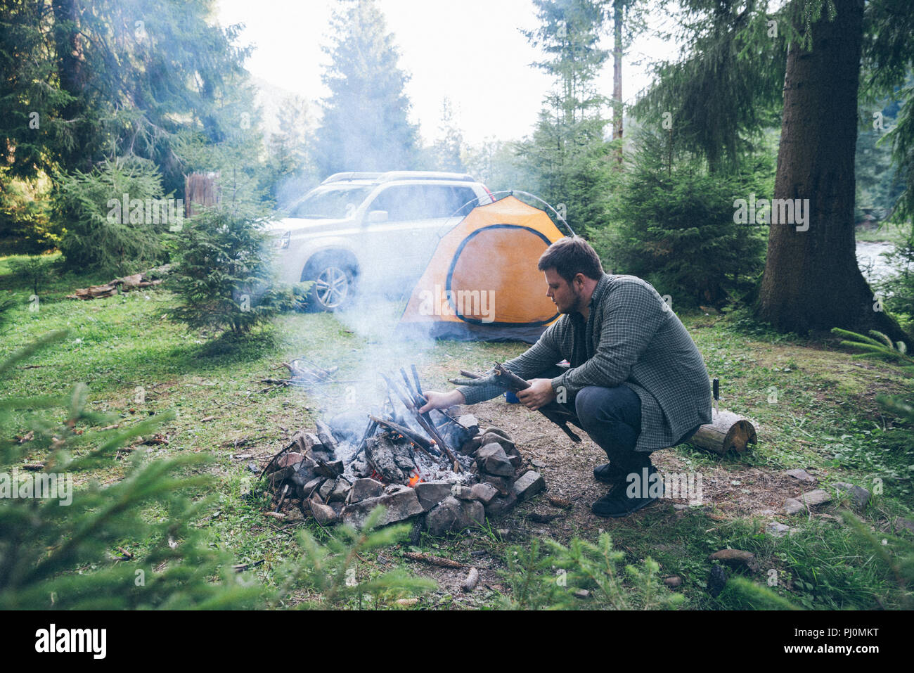 man build fire in forest, car with yellow tent on background. camping ...
