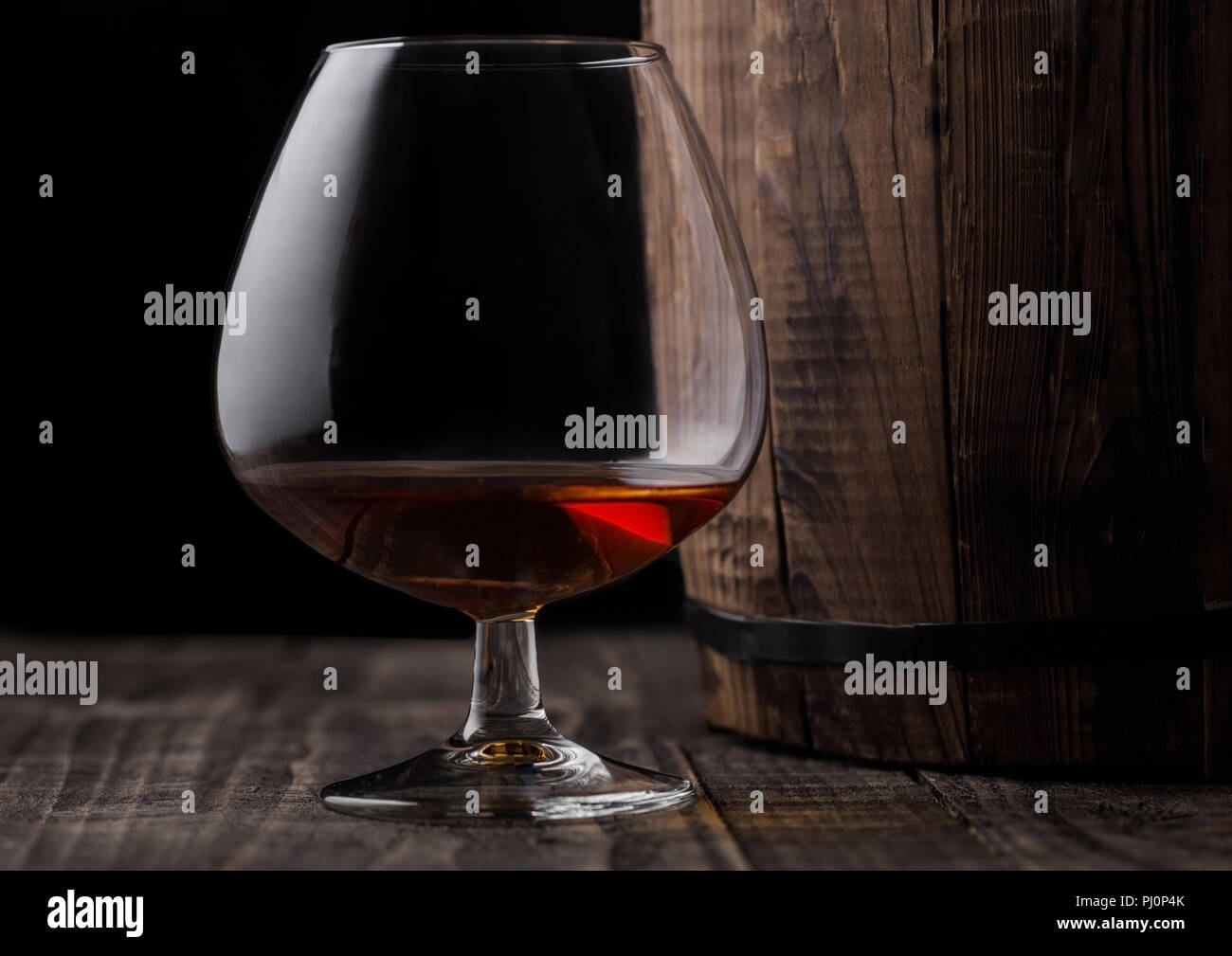 Glass of cognac brandy drink next to wooden barrel on black background ...