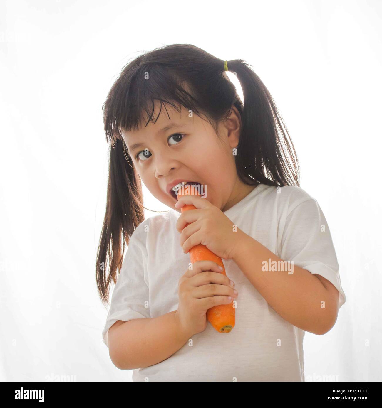 Carrot in hand kid, little girl bitting carrot on white background ...