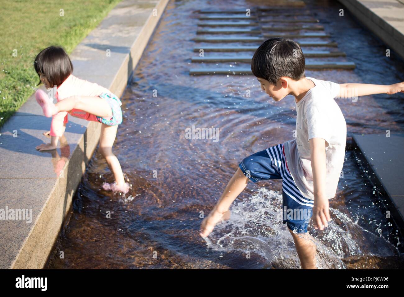 An Asian boy and girl are kicking off water of stream and make splash ...
