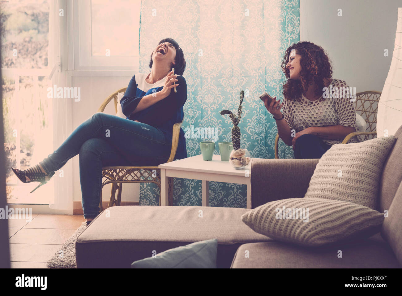 two young happy women friends sit down at home and laugh telling ...