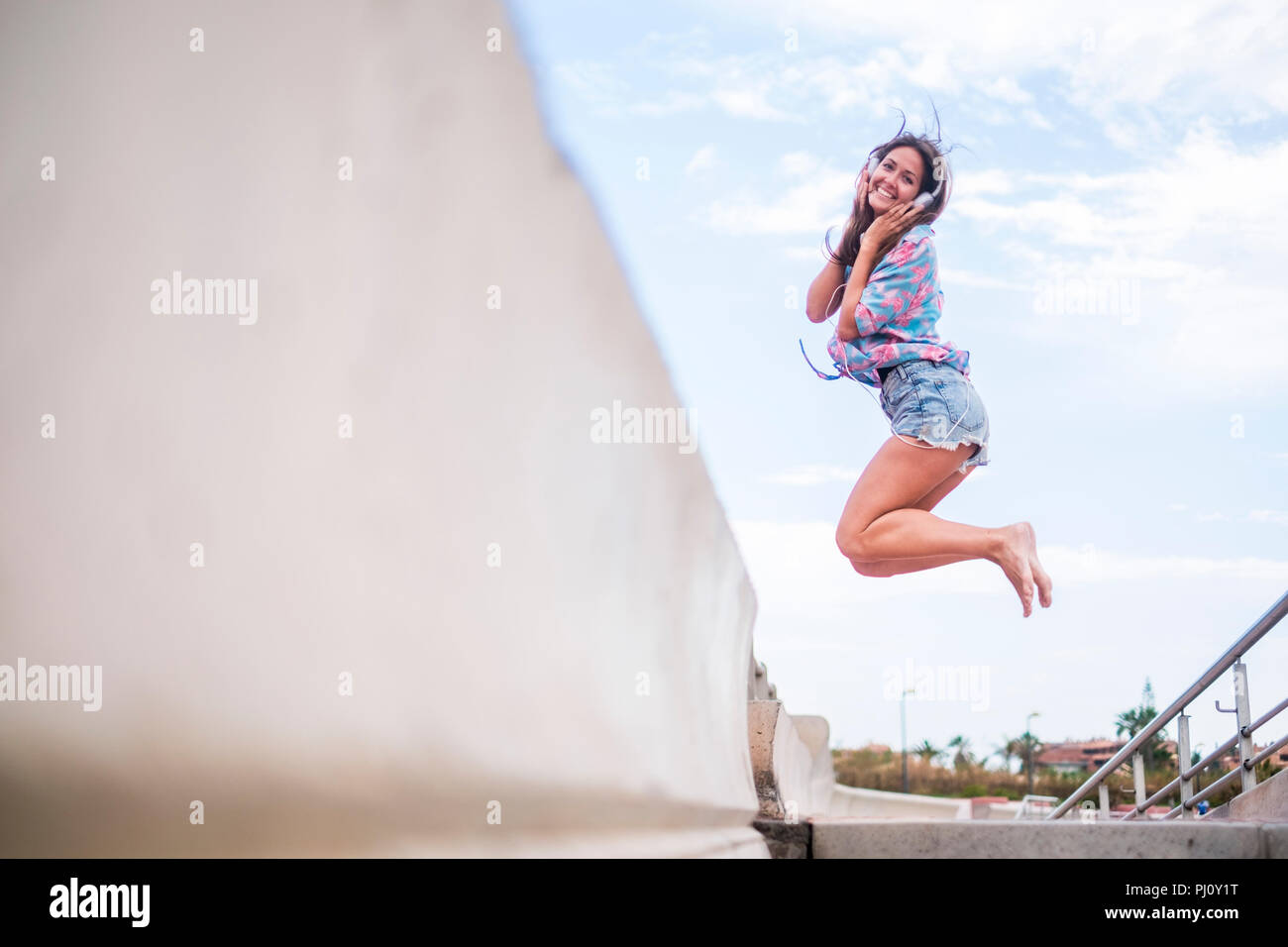 Happiness concept with young beautiful girl jumping with joyful against a white sky blue ...
