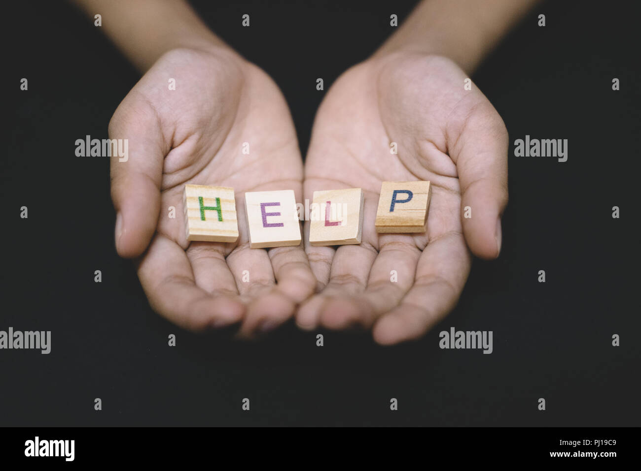 wooden alphabet tiles word HELP in a child hand over dark background ...