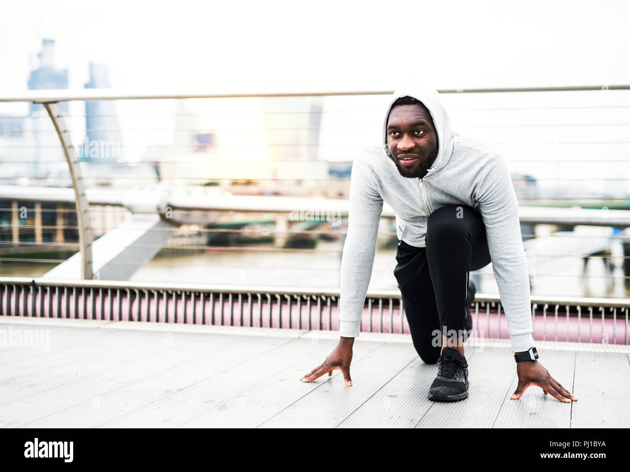 Young sporty black man runner in starting position on the bridge in a ...