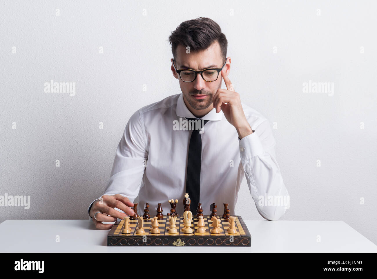 Portrait of a young man in a studio, sitting at the table with chess ...