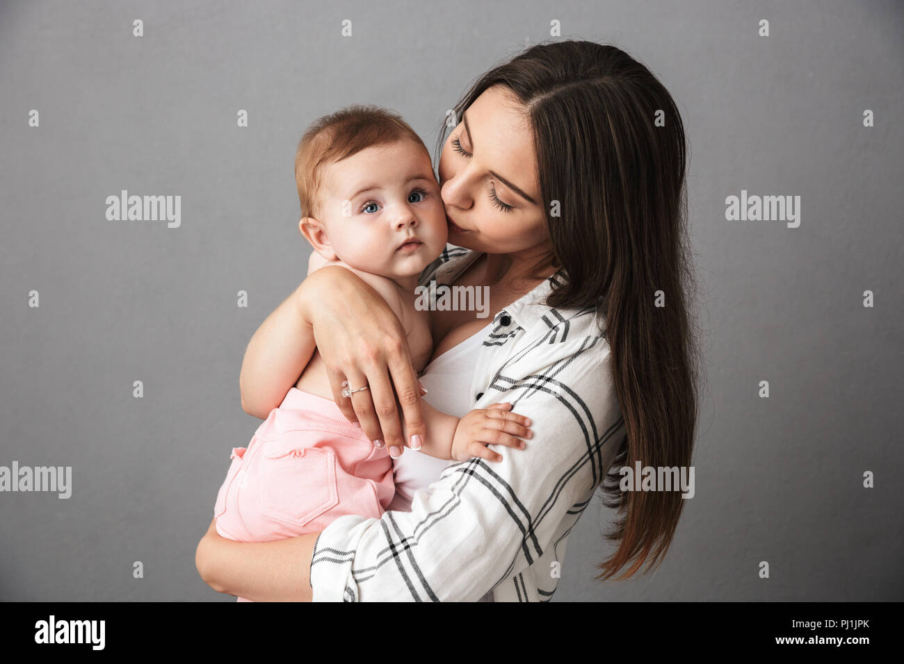 Portrait of a smiling young mother holding her little baby girl over gray background Stock Photo ...