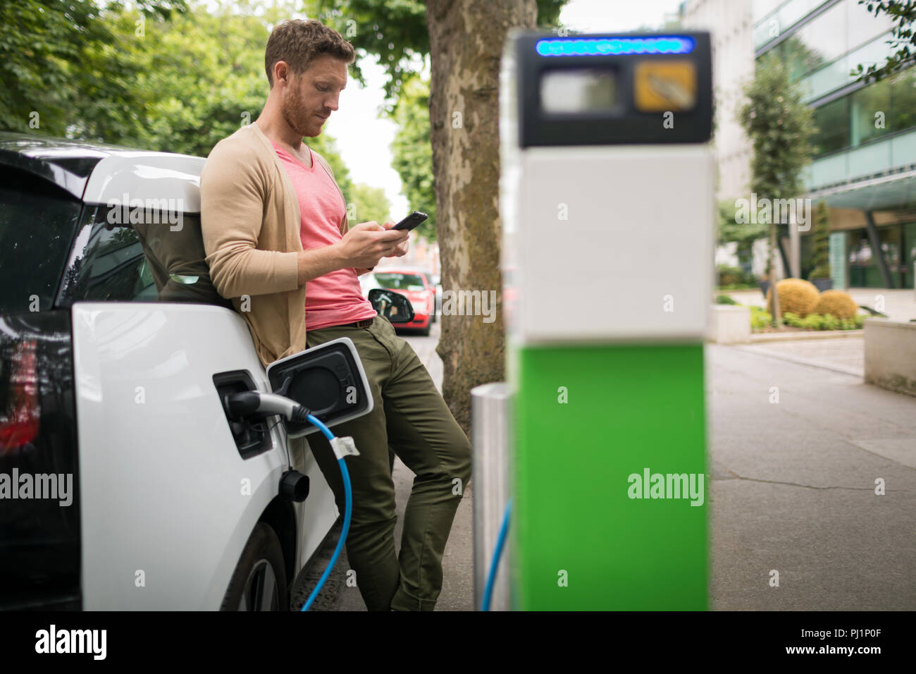 Man using mobile phone while charging electric car Stock Photo - Alamy