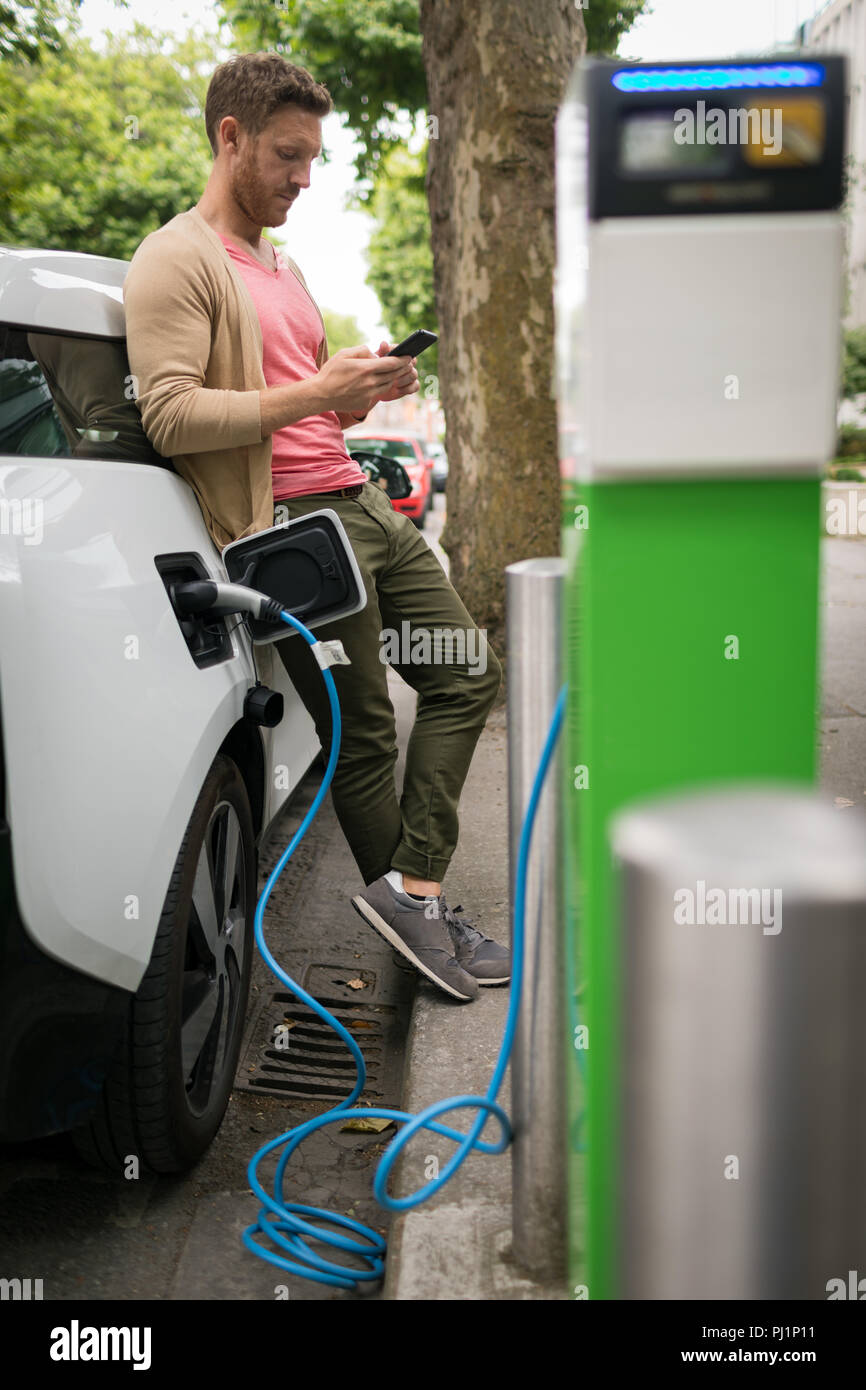Man using mobile phone while charging electric car Stock Photo - Alamy