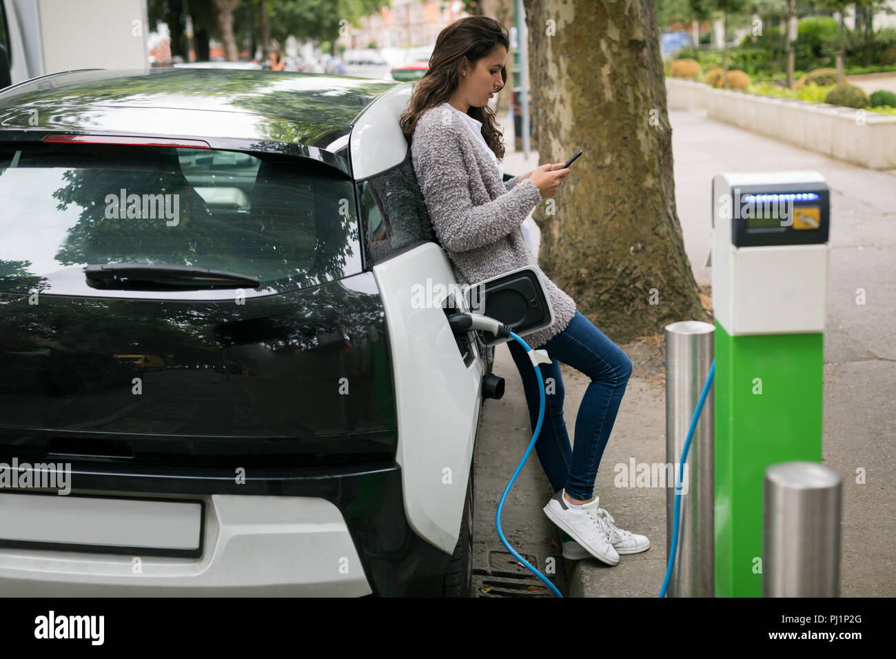 Woman using mobile phone while charging electric car Stock Photo - Alamy