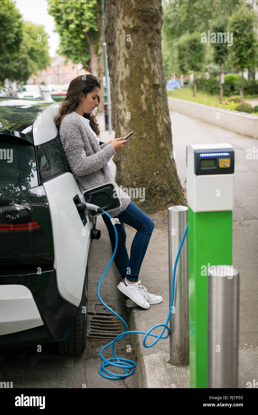 Woman using mobile phone while charging electric car Stock Photo - Alamy