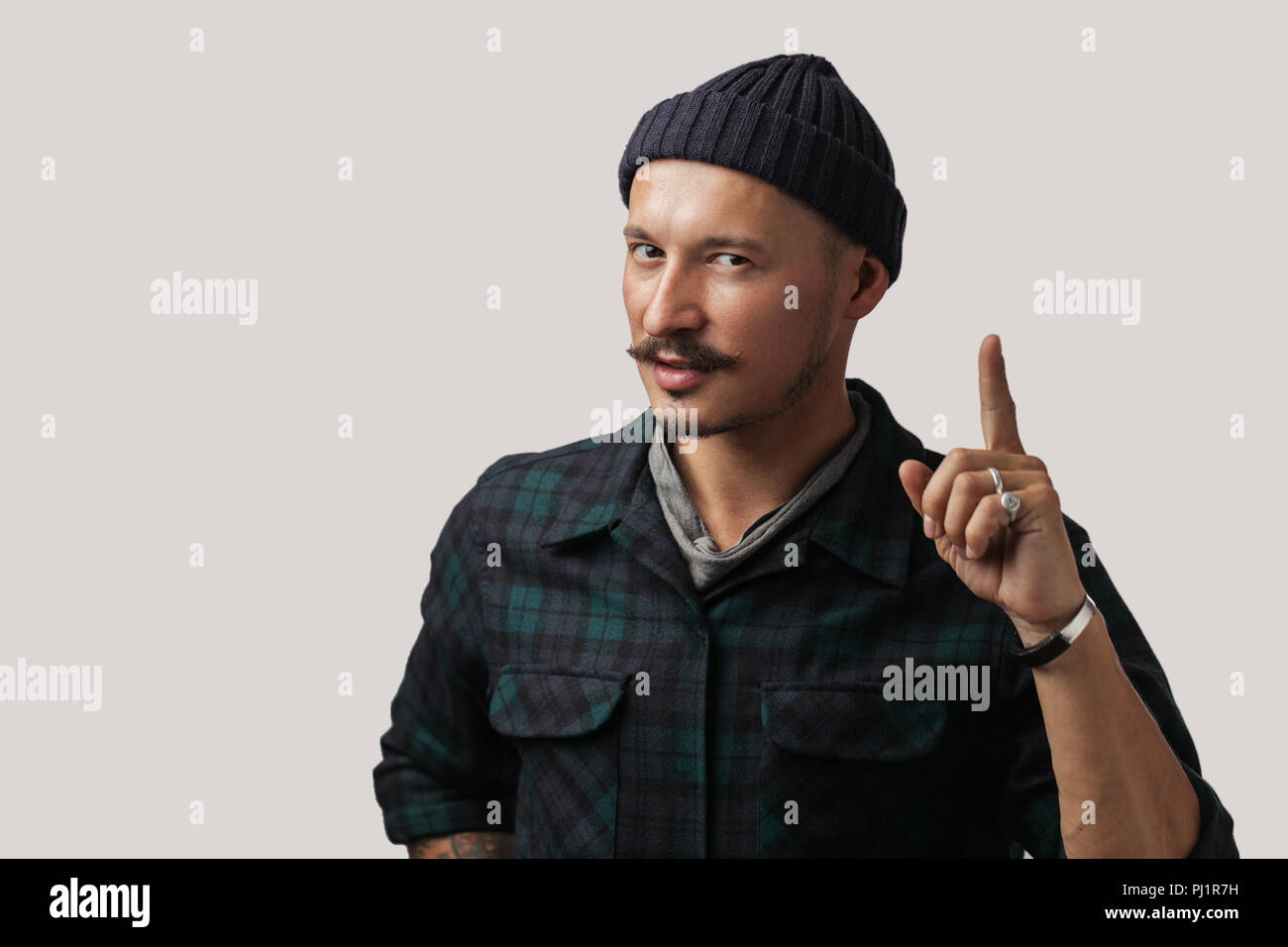 Confident man in knitted hat pointing finger upwards over white ...