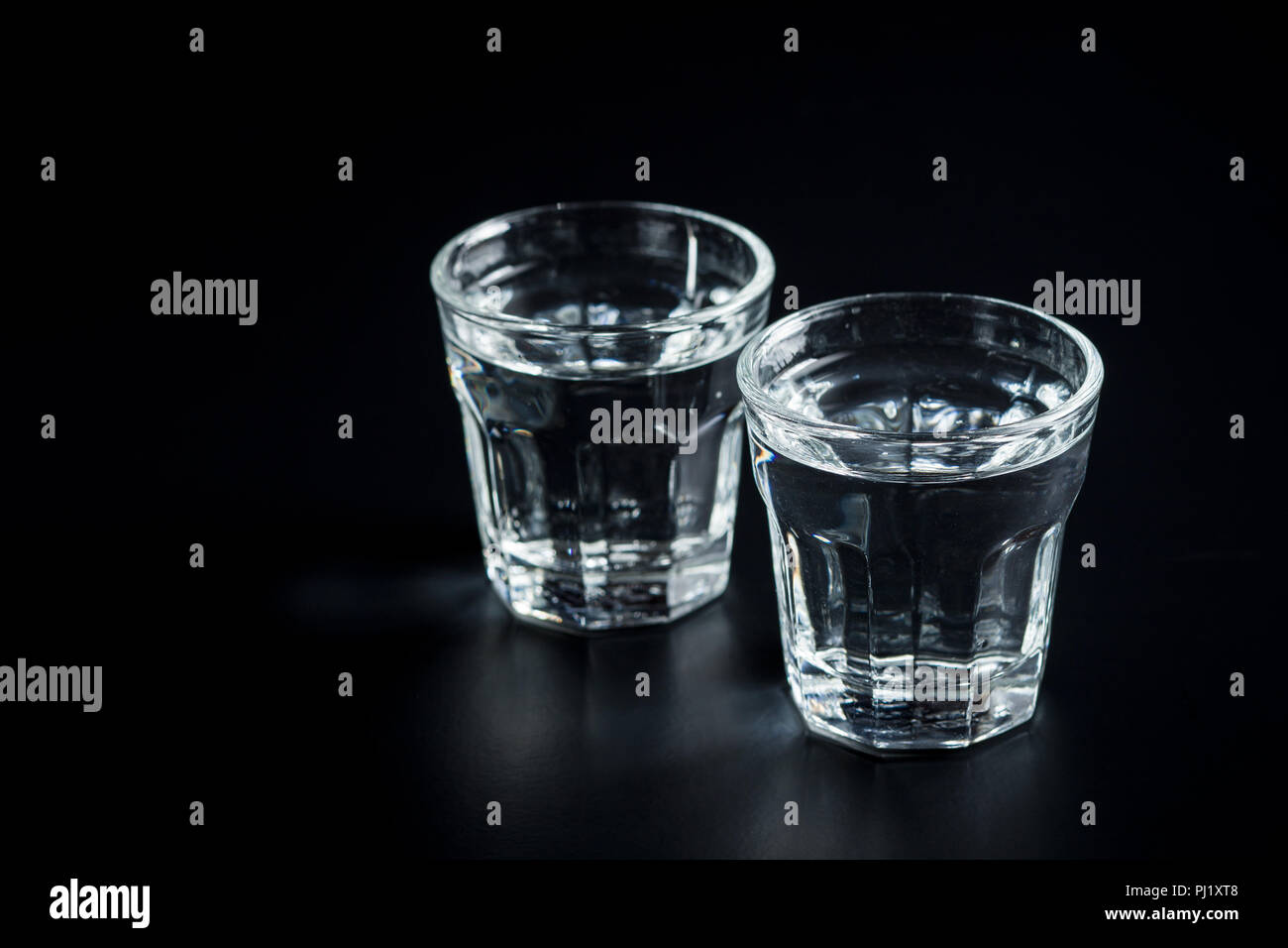 Vodka in shot glass. Transparent alcohol on black table Stock Photo - Alamy
