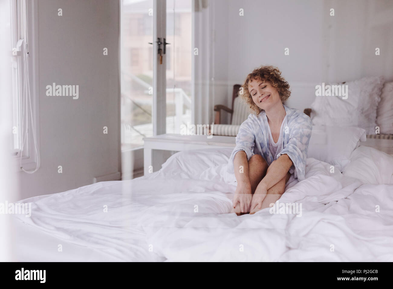 Happy woman sitting on bed after waking up in the morning. Woman waking ...