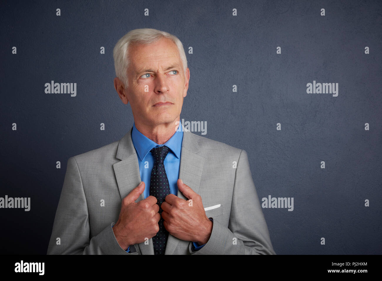 Studio portrait of elderly man wearing suit while standing at grey ...