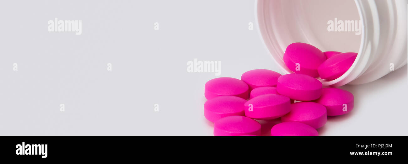 Brightly pink tablets scatter from a white bottle. Side view. Close-up ...