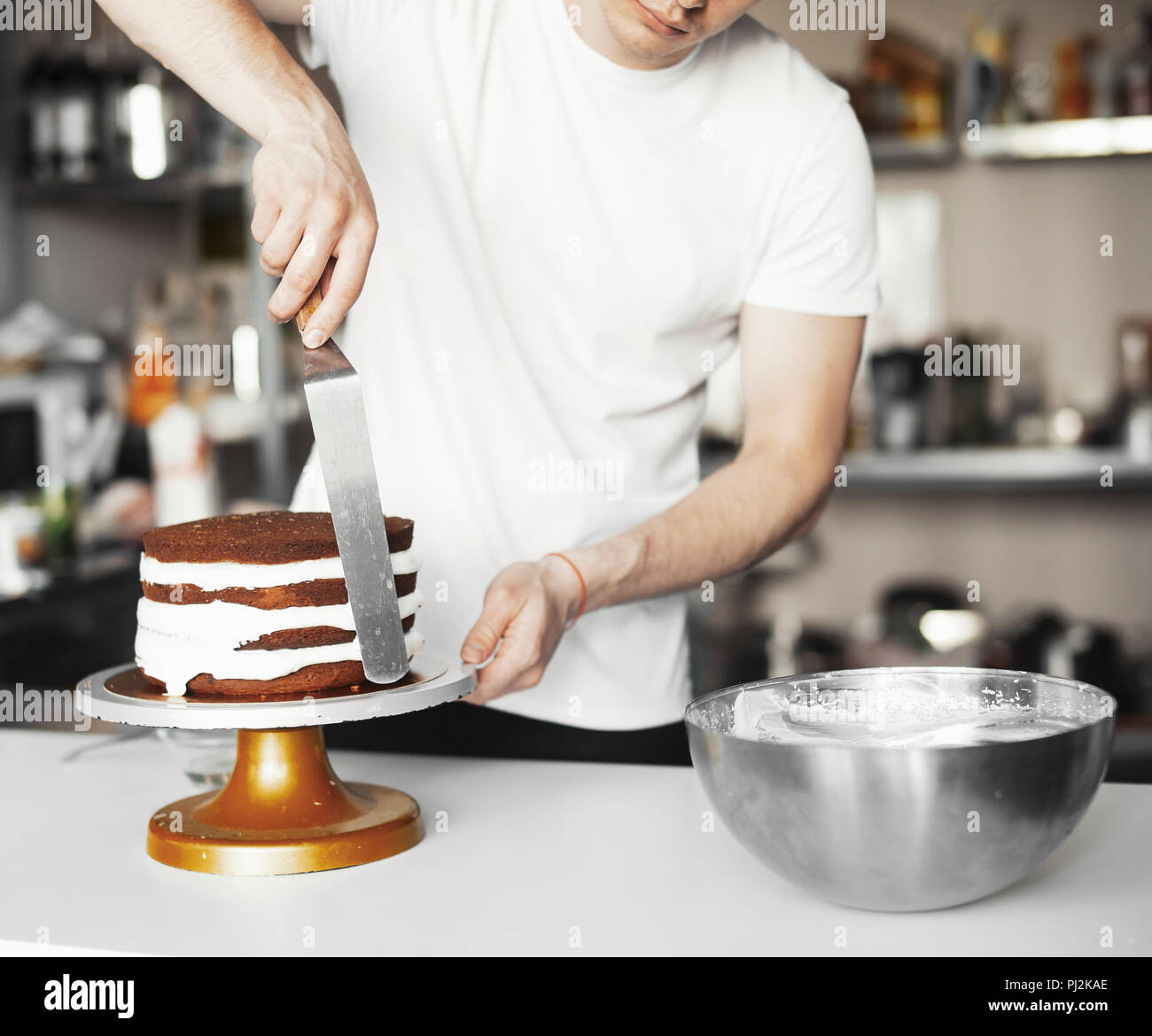 Close up of young man smearing cream on chocolate cake by metal spatula ...