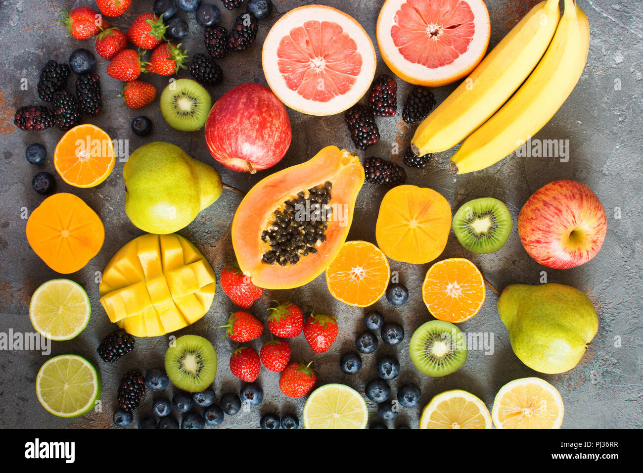 Different rainbow colored fruits on the grey concrete background, top ...