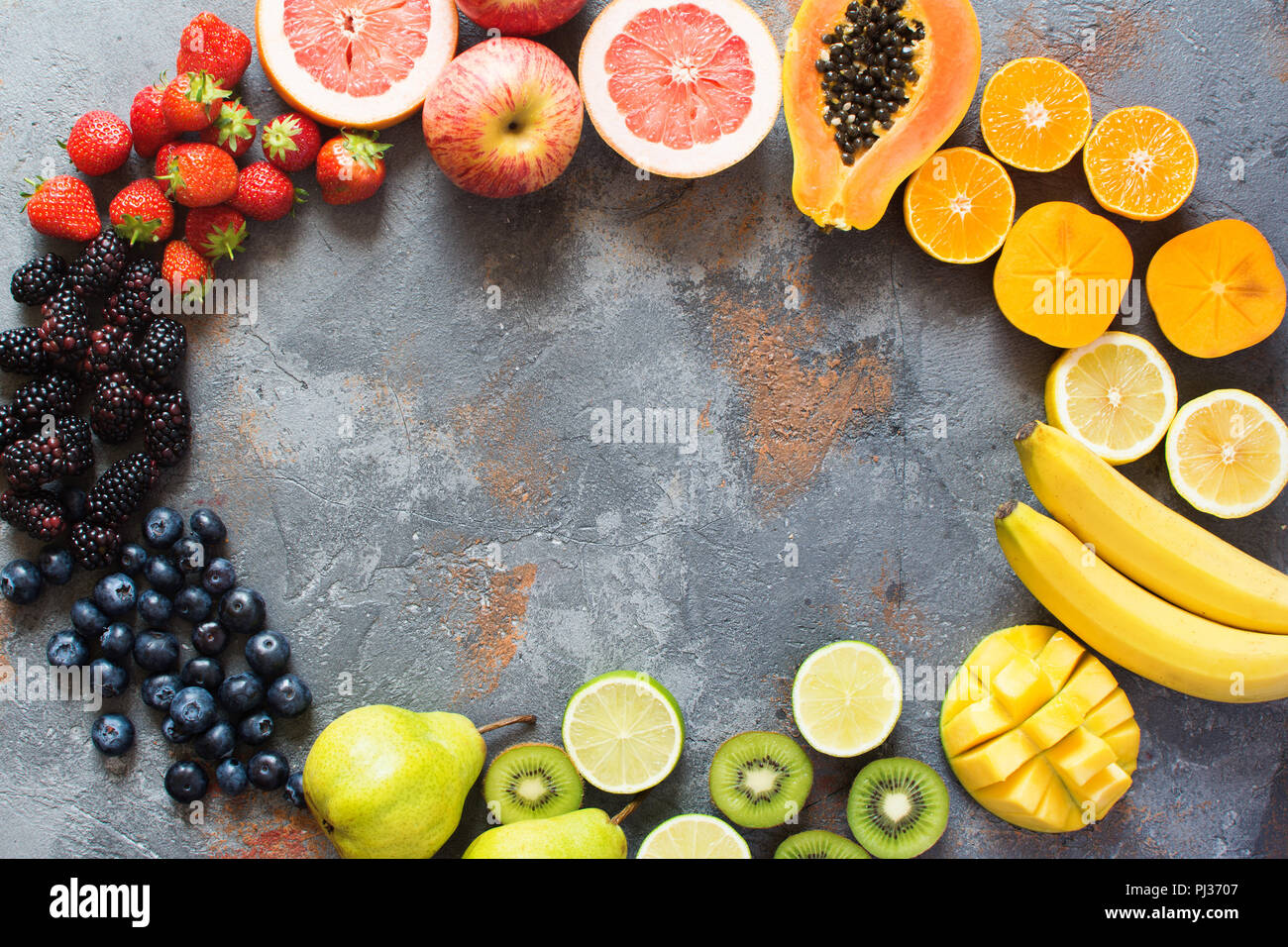Rainbow colored fruits and berries arranged in a circle, on the grey ...