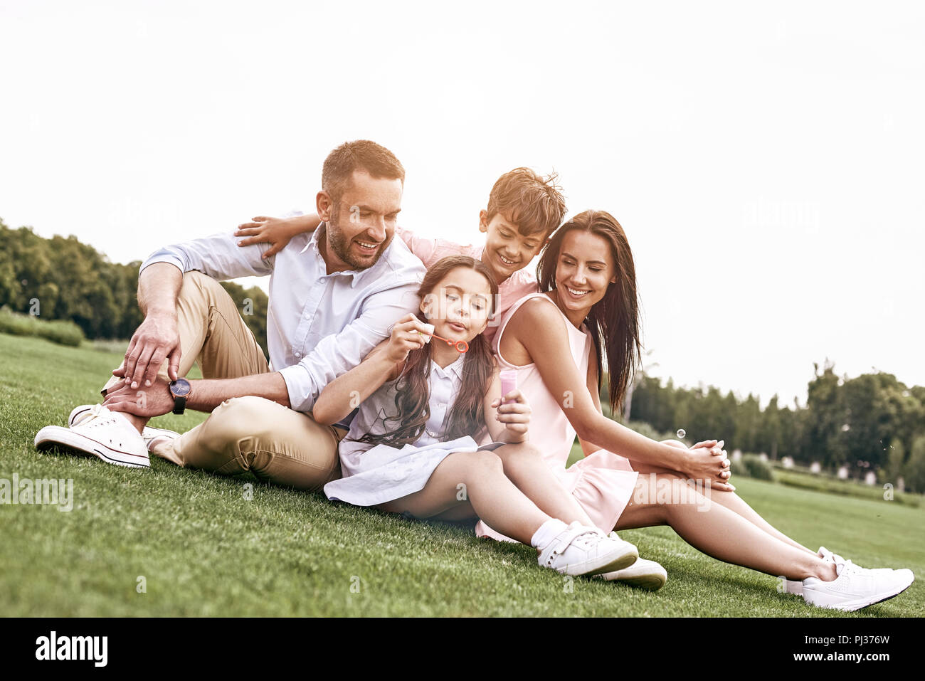 Bonding. Family of four sitting on a grassy field blowing bubble Stock ...