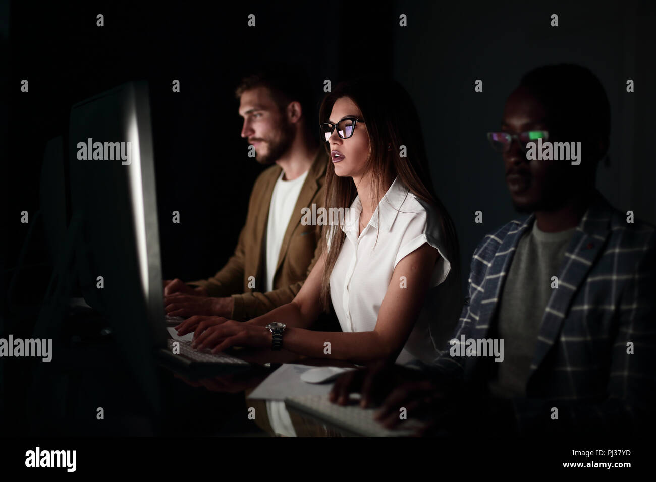 financial team sitting in an office in front of a computer at night ...