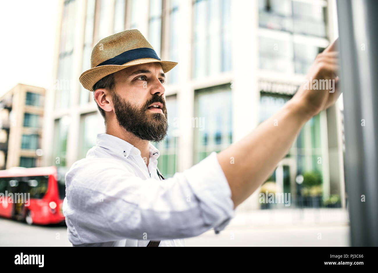 Hipster man tourist waiting for the bus in the city, checking timetable ...