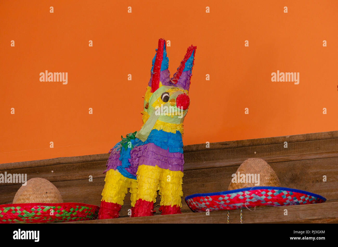 Colorful Piñata and hats on display shelf mounted on orange wall Stock ...