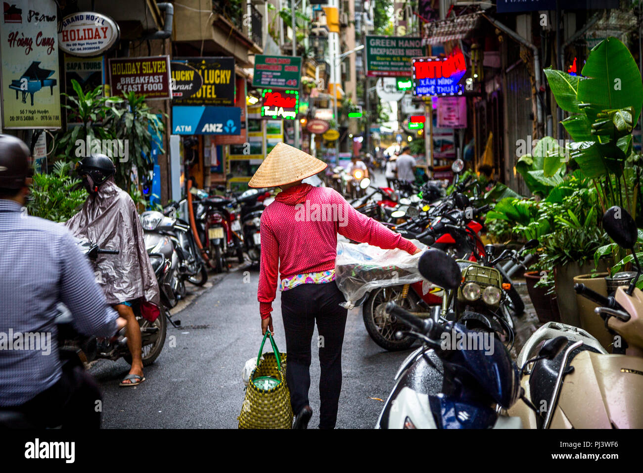 Crowded alley centered on Asian lady wearing hat and red top and ...