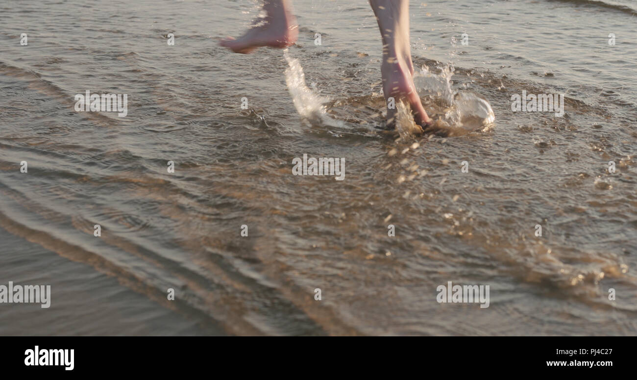closeup of man legs running in shallow water on a beach on sunny day ...