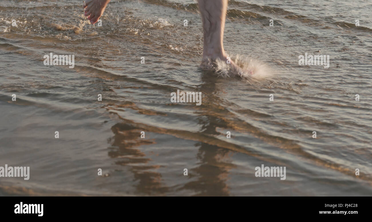 closeup of man legs running in shallow water on a beach on sunny day ...